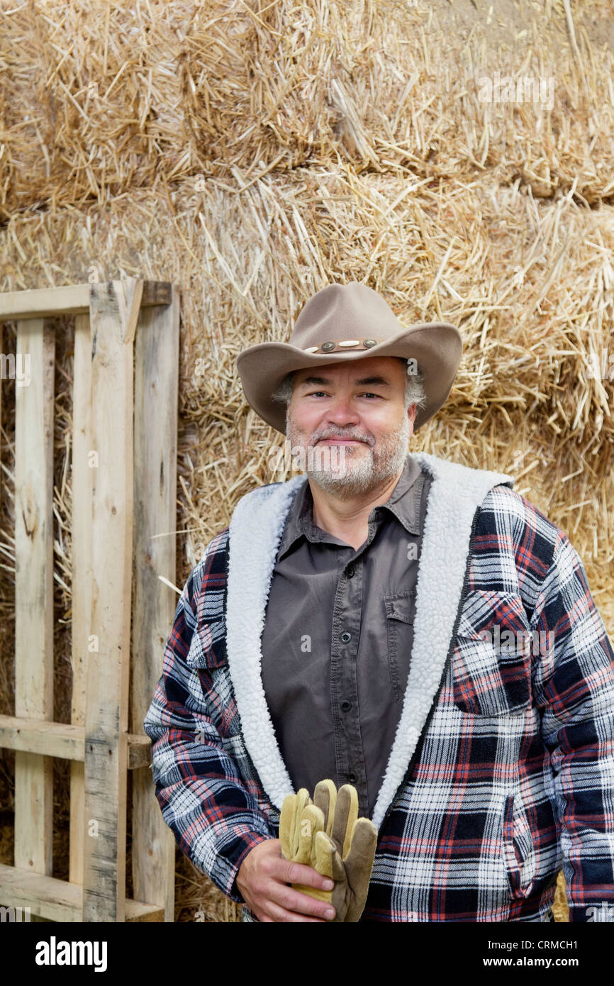 Portrait of a happy mature man with cowboy hat holding gloves in front ...