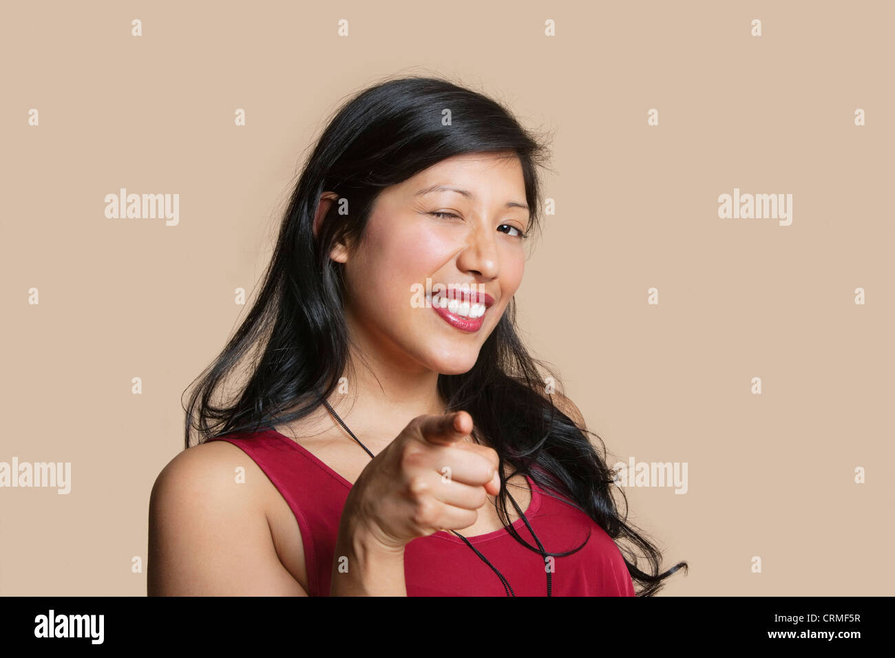 Portrait of a young woman pointing while winking over colored ...