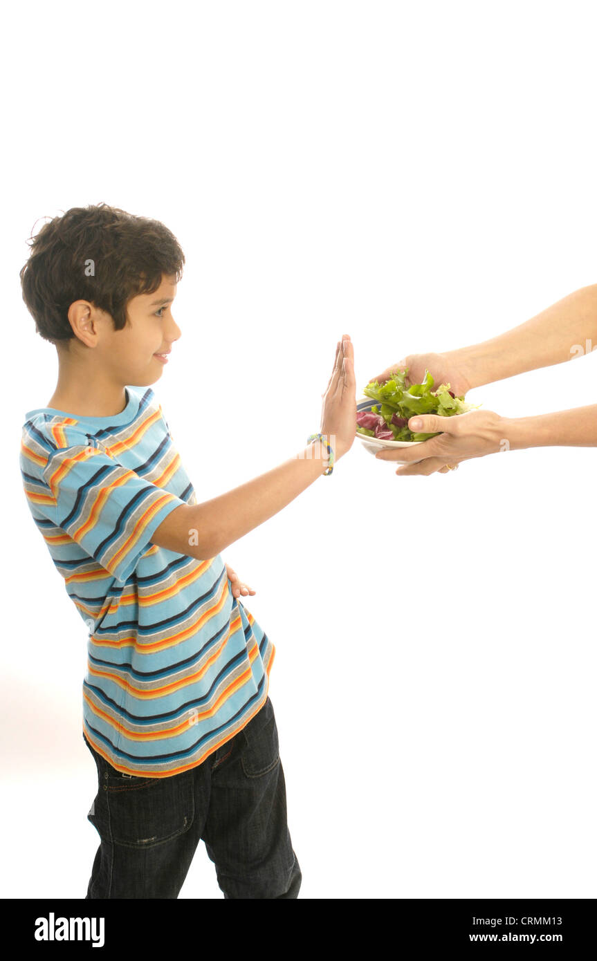 A young boy refusing to eat a bowl of salad, given to him by his mother ...