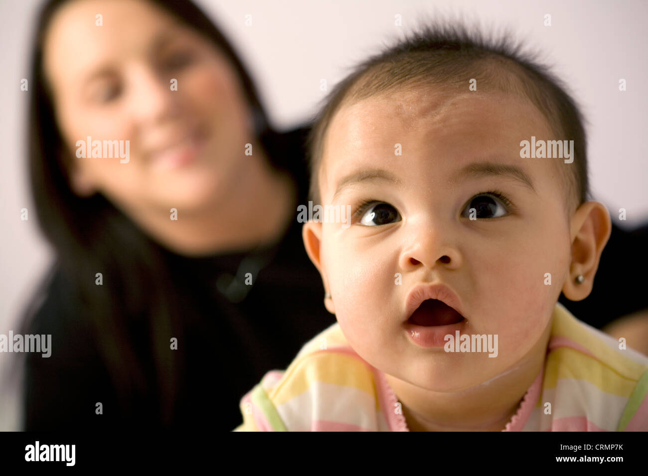 A happy baby girl sitting up right. Mother can be seen in background ...