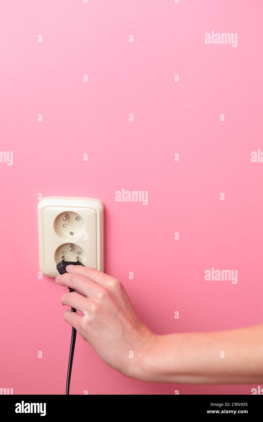 Young woman's hand plugging a power plug into an electric wall socket ...