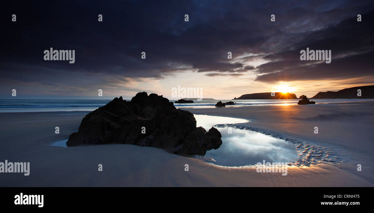 The last rays of sunlight bathe a beach in warm light minutes before ...