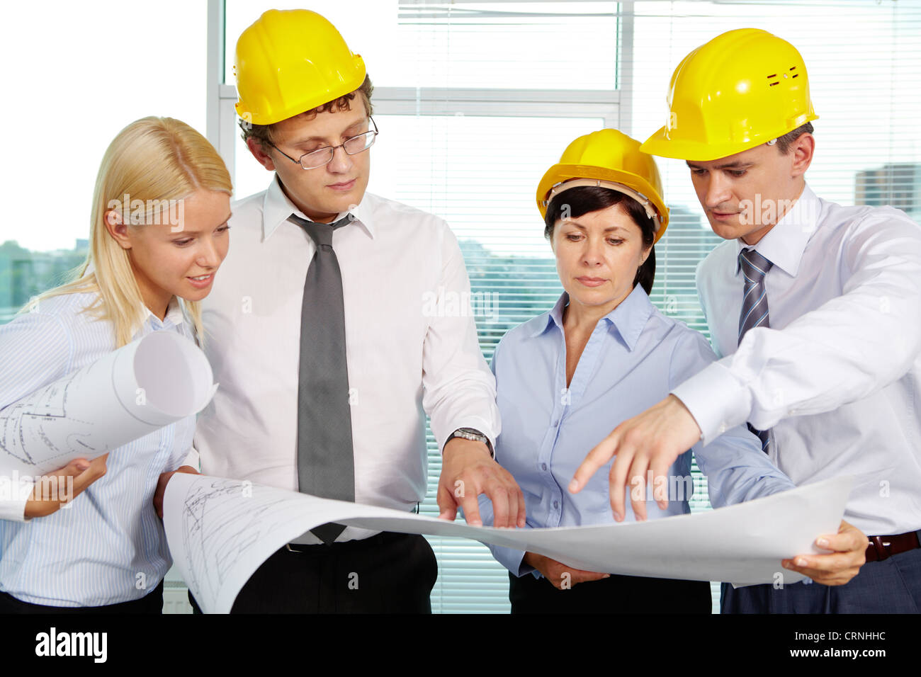 Team of four engineers discussing the blueprint held by one of them ...