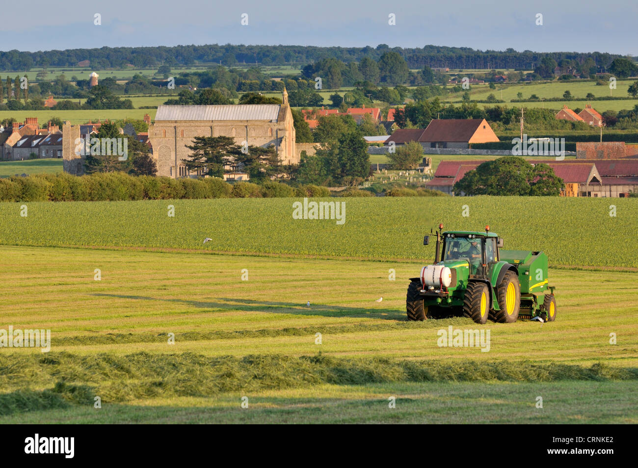 Tractor baling forage hay with Binham priory and village in the ...