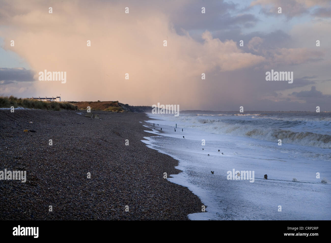 View of incoming tide over shingle beach, with stormclouds over old ...