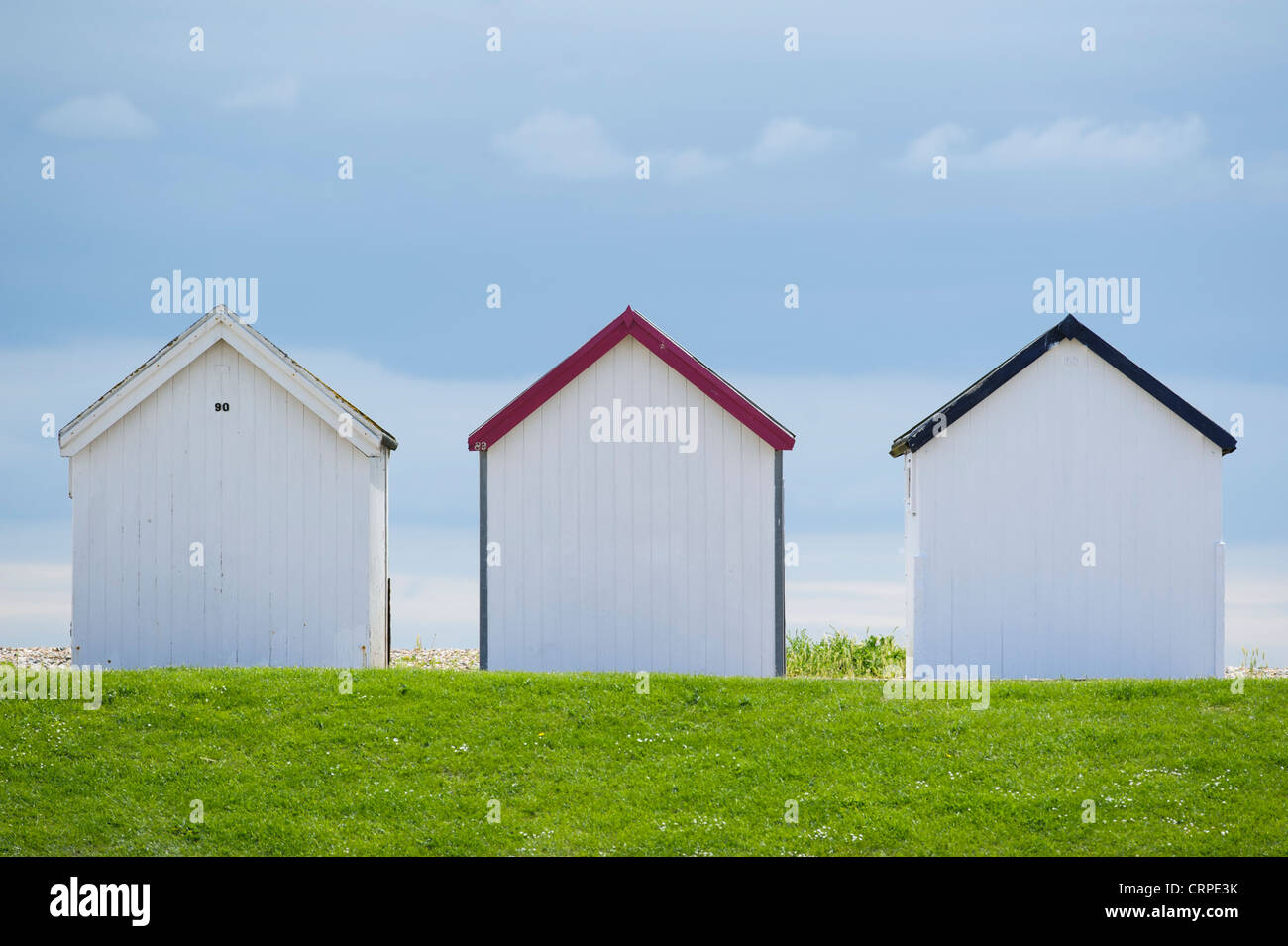 Three English beach huts sitting between the beach and a grass hill ...