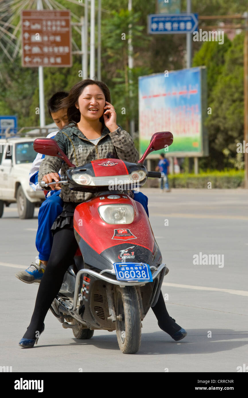 A Chinese woman travels along a road on her scooter while talking on ...