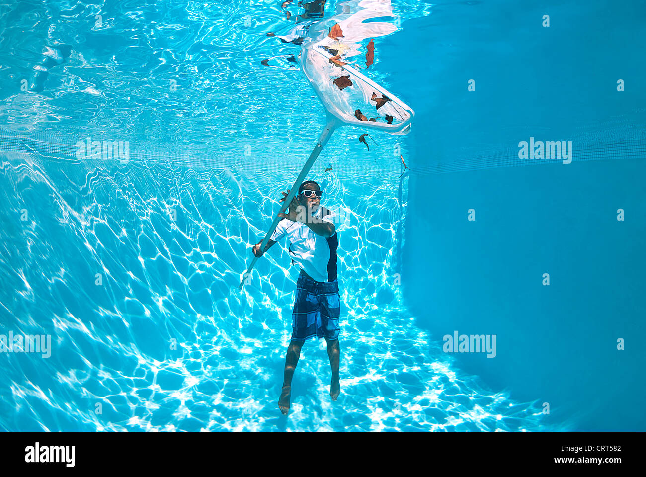 Young man is cleaning the swimming pool from underwater with a skimmer ...