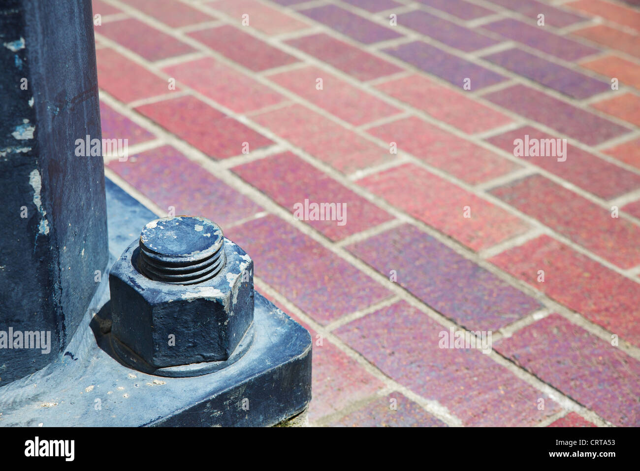 Close up of a lamp post bolt and nut with soft focus brick sidewalk ...