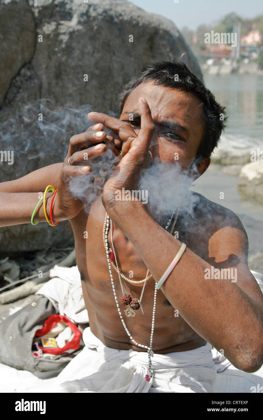 An Indian Sadhu smokes hashish from a pipe next to the River Ganges in ...