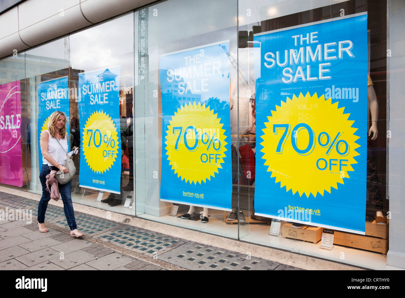 Woman walks past 70 per cent reduction summer sales posters of a Burton ...