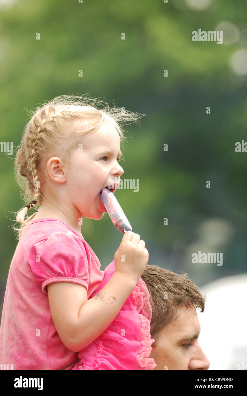 Young girl sitting on her father's shoulders eating a Popsicle Stock ...