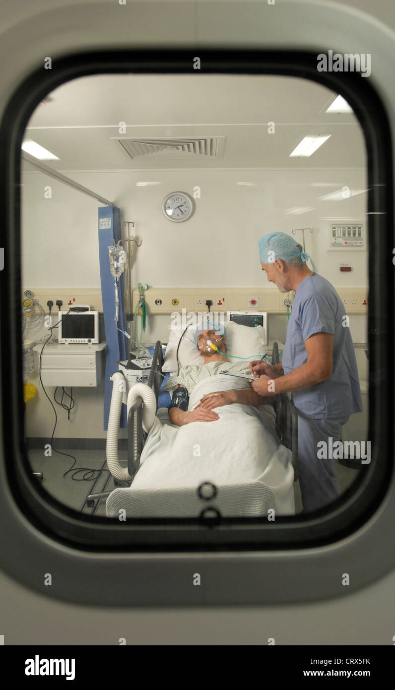 Through the window of a hospital ward, doctors can be seen talking to a ...