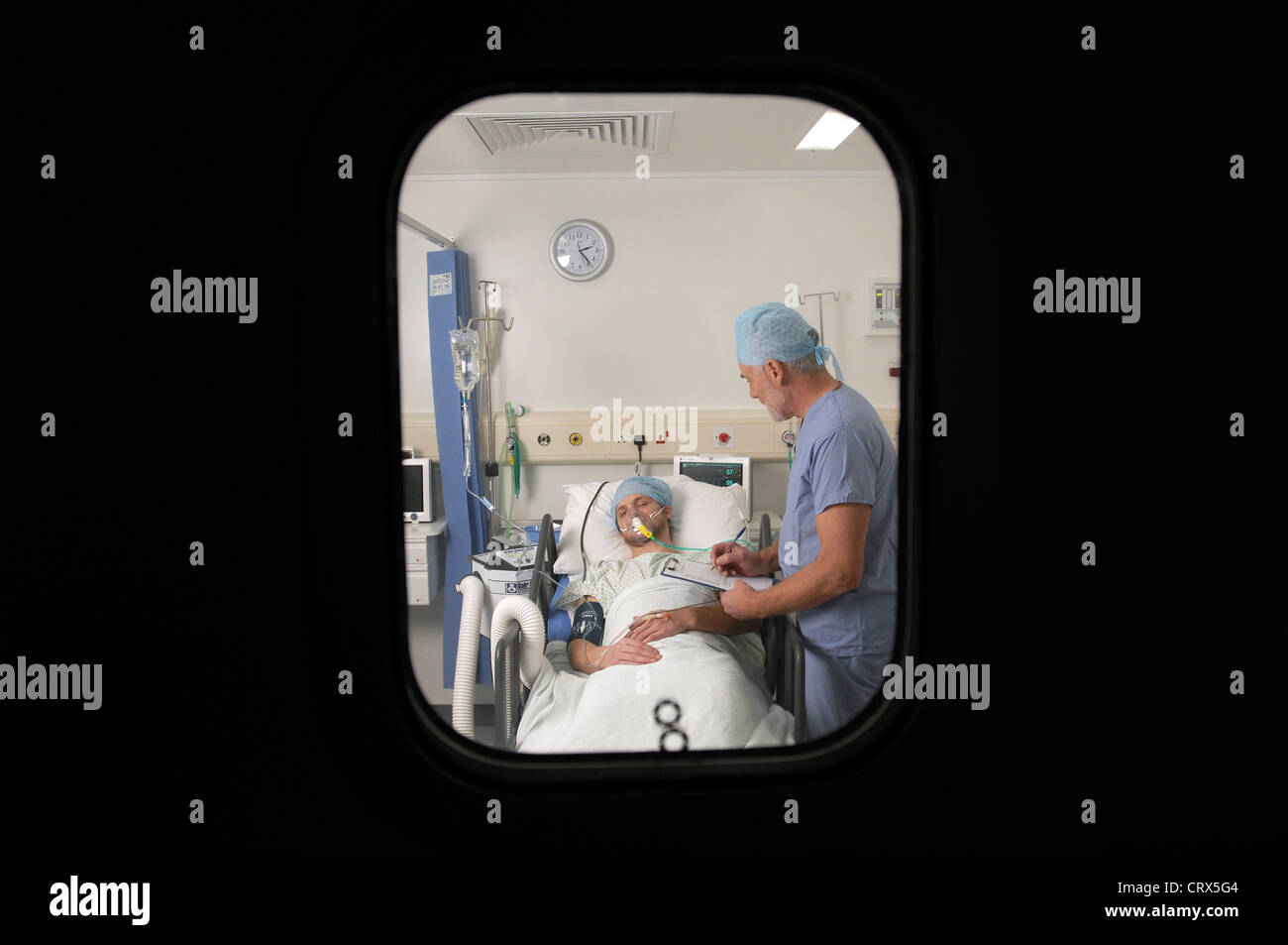 Through the window of a hospital ward, doctors can be seen talking to a ...
