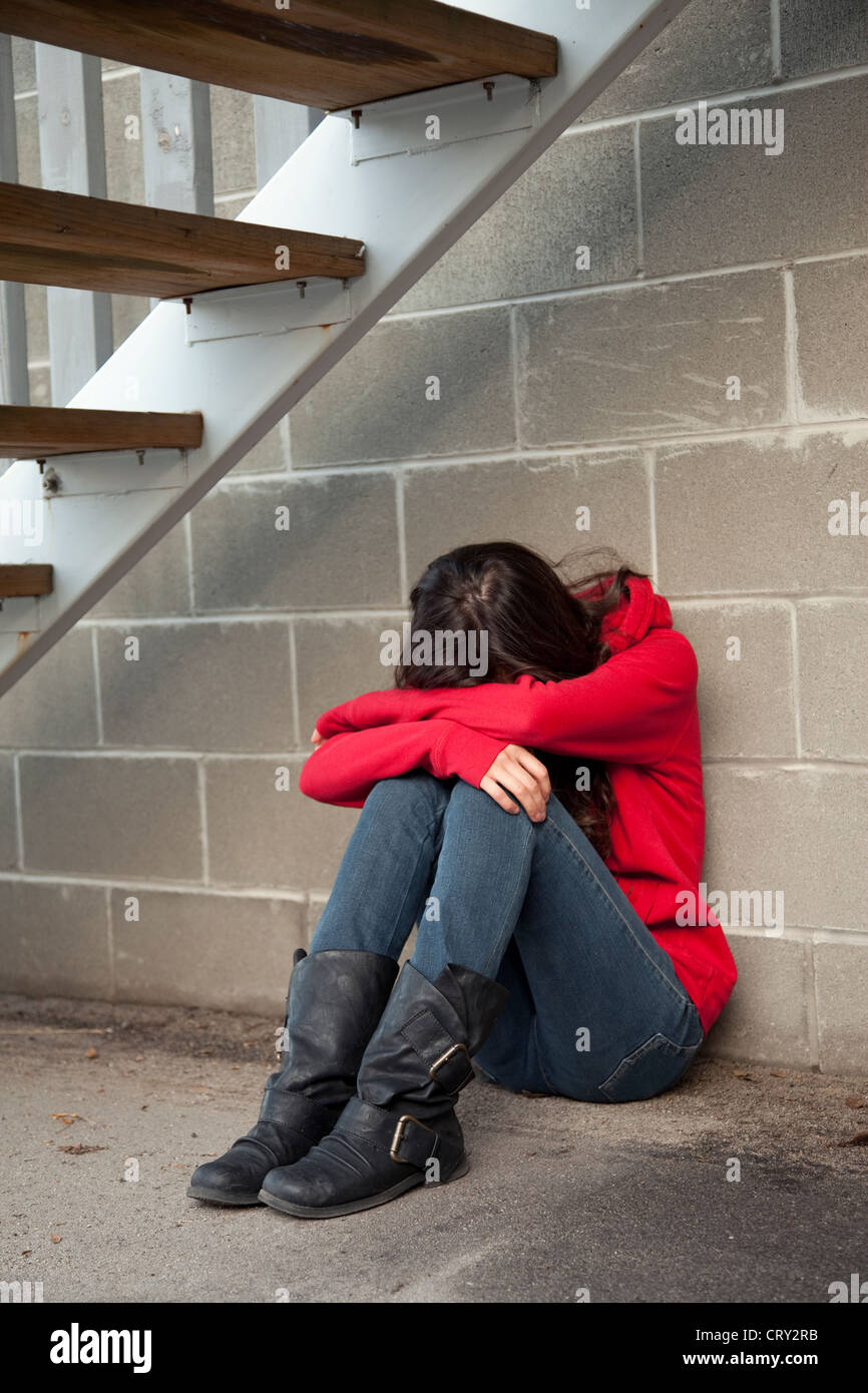 Teenage girl sitting under staircase in alley-way in a depressed state ...