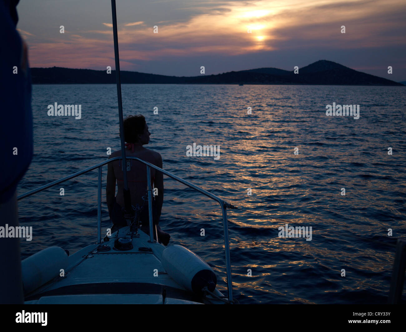 A girl sitting on a pulpit of a sailing boat at sunset Stock Photo - Alamy