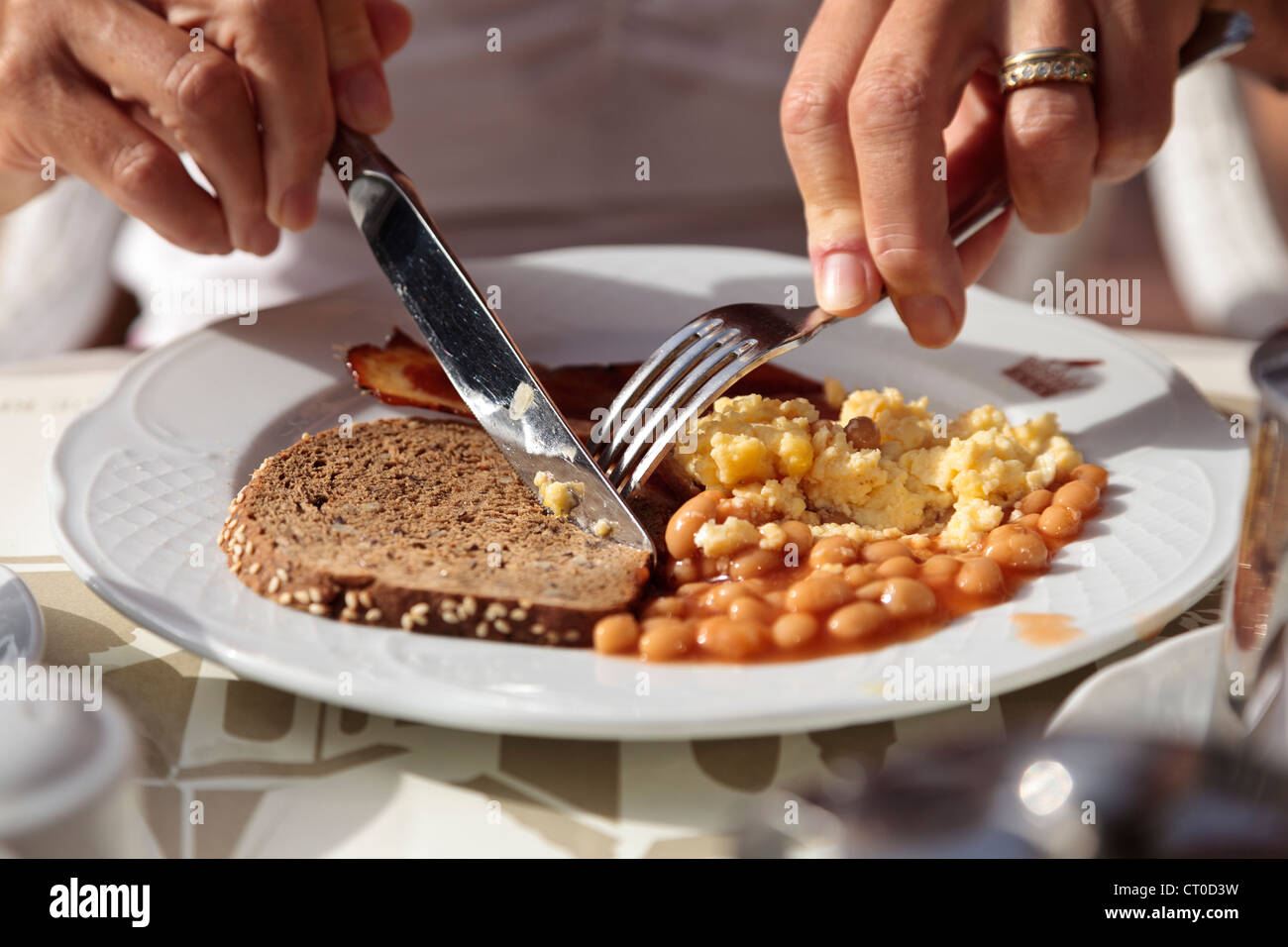 Breakfast plate of toast, beans, scrambled eggs and bacon being eaten ...