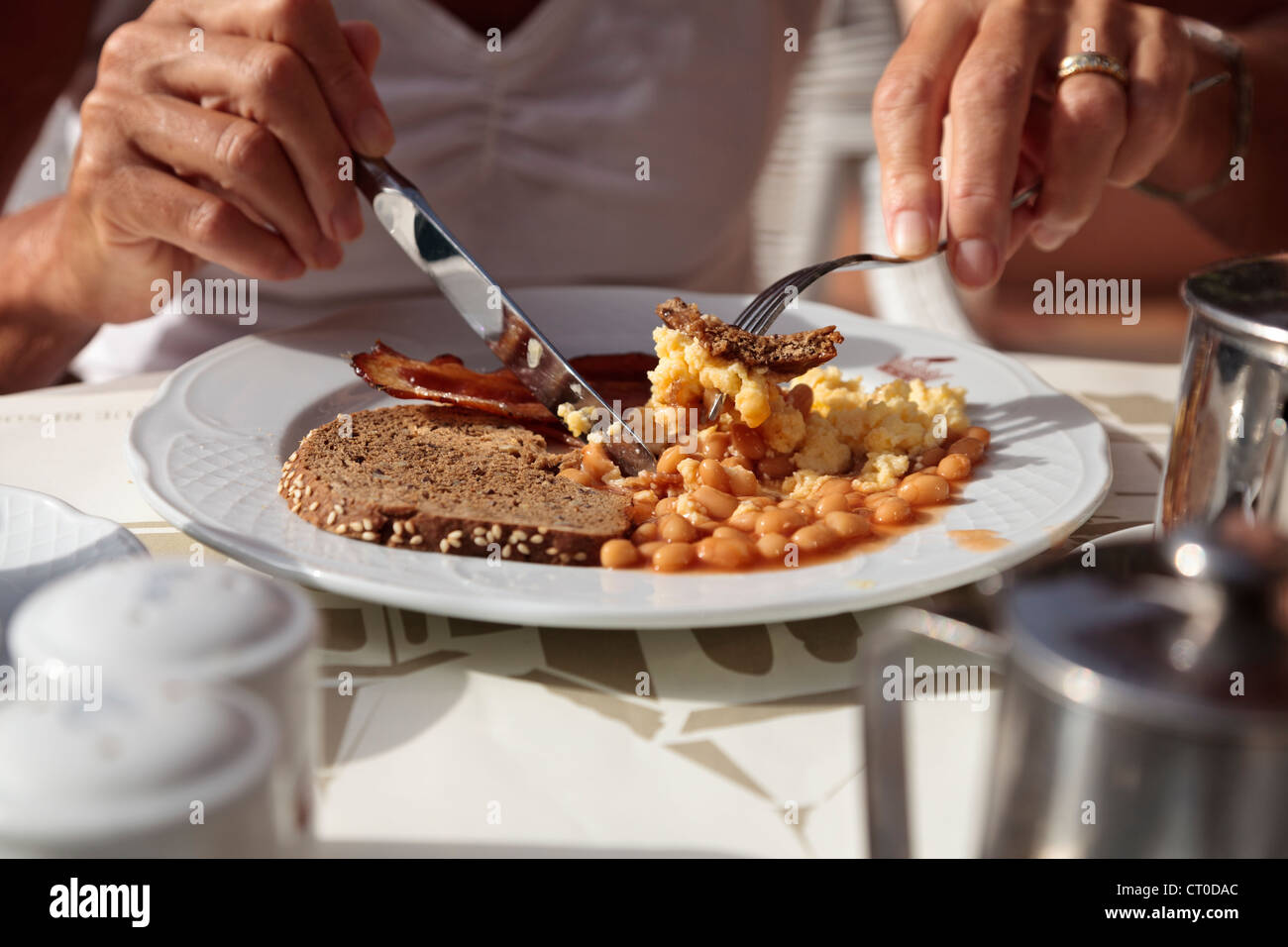 Breakfast plate of toast, beans, scrambled eggs and bacon being eaten ...