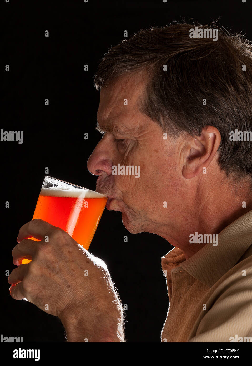 Senior caucasian man in profile drinking from a pint glass of beer or ...