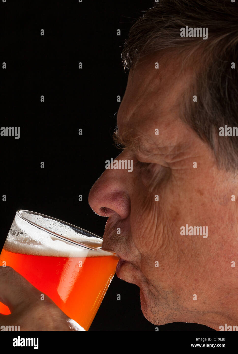 Senior caucasian man in profile drinking from a pint glass of beer or ...
