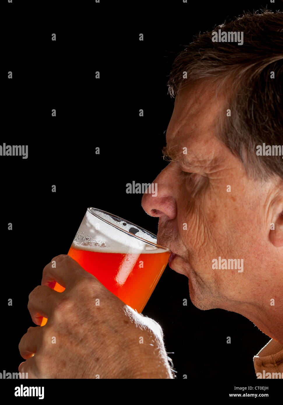 Senior caucasian man in profile drinking from a pint glass of beer or ...