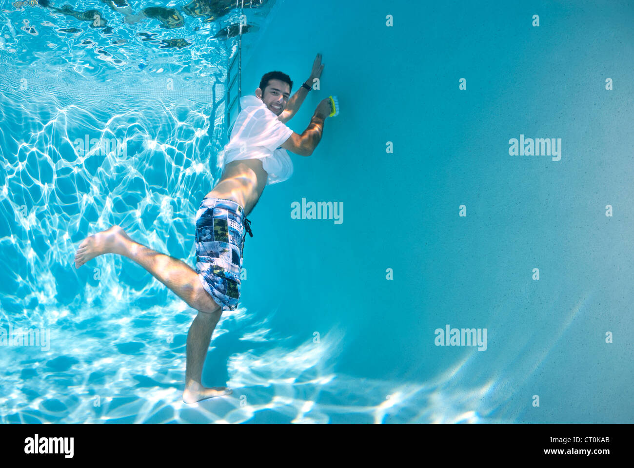 Young man is cleaning the swimming pool from underwater with a brush ...