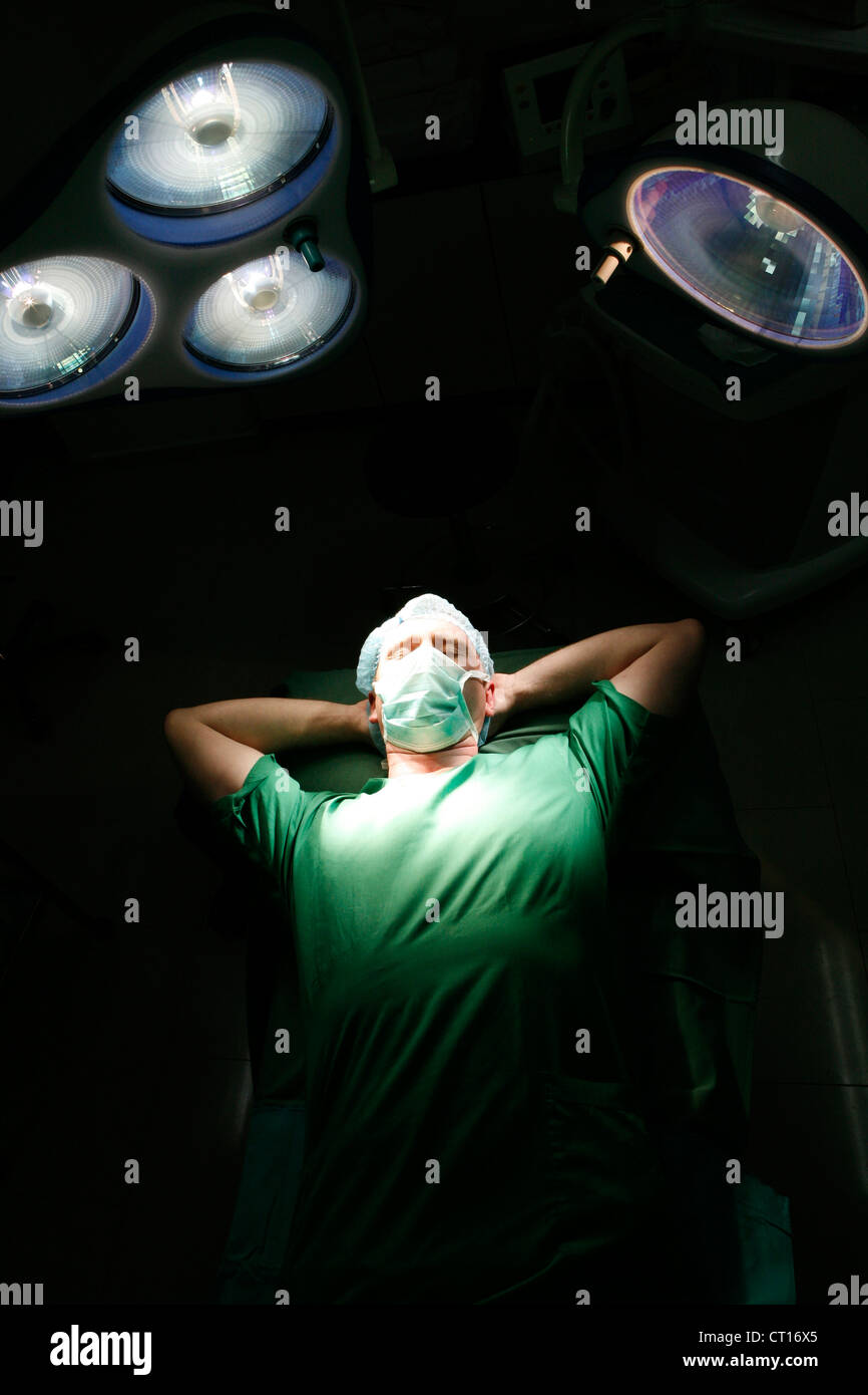 A tired Surgeon sleeps on an operating table with his hands behind his ...