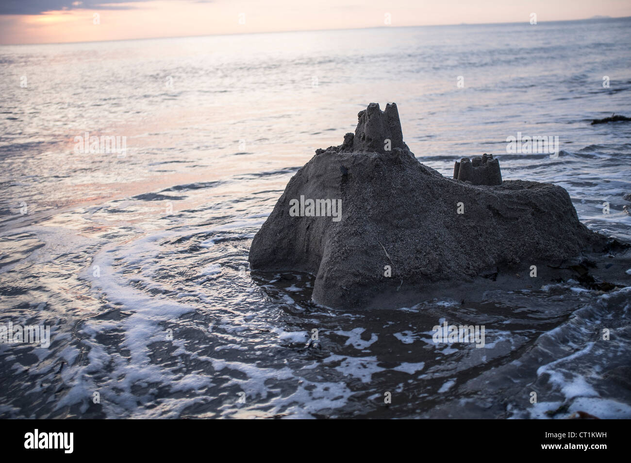 waves lapping around a sandcastle on a beach at sunset, cardigan bay ...