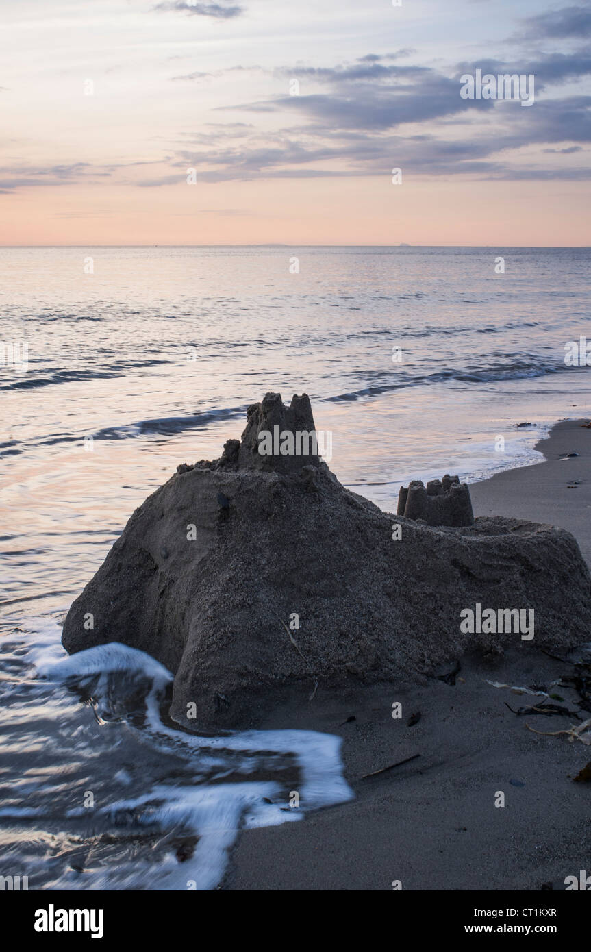 waves lapping around a sandcastle on a beach at sunset, cardigan bay ...