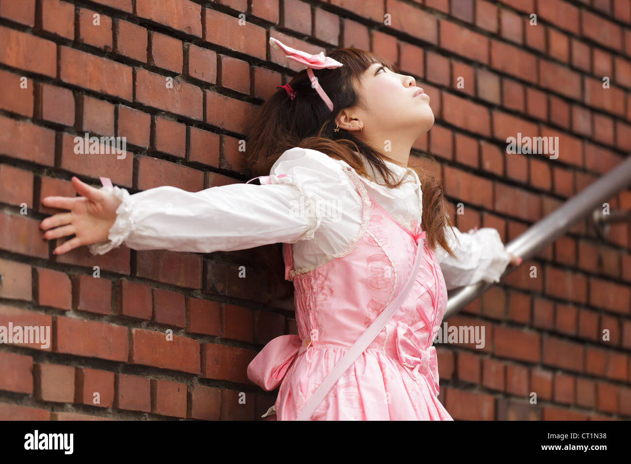 stressed japanese lolita cosplay leaning against brick wall on stairs ...
