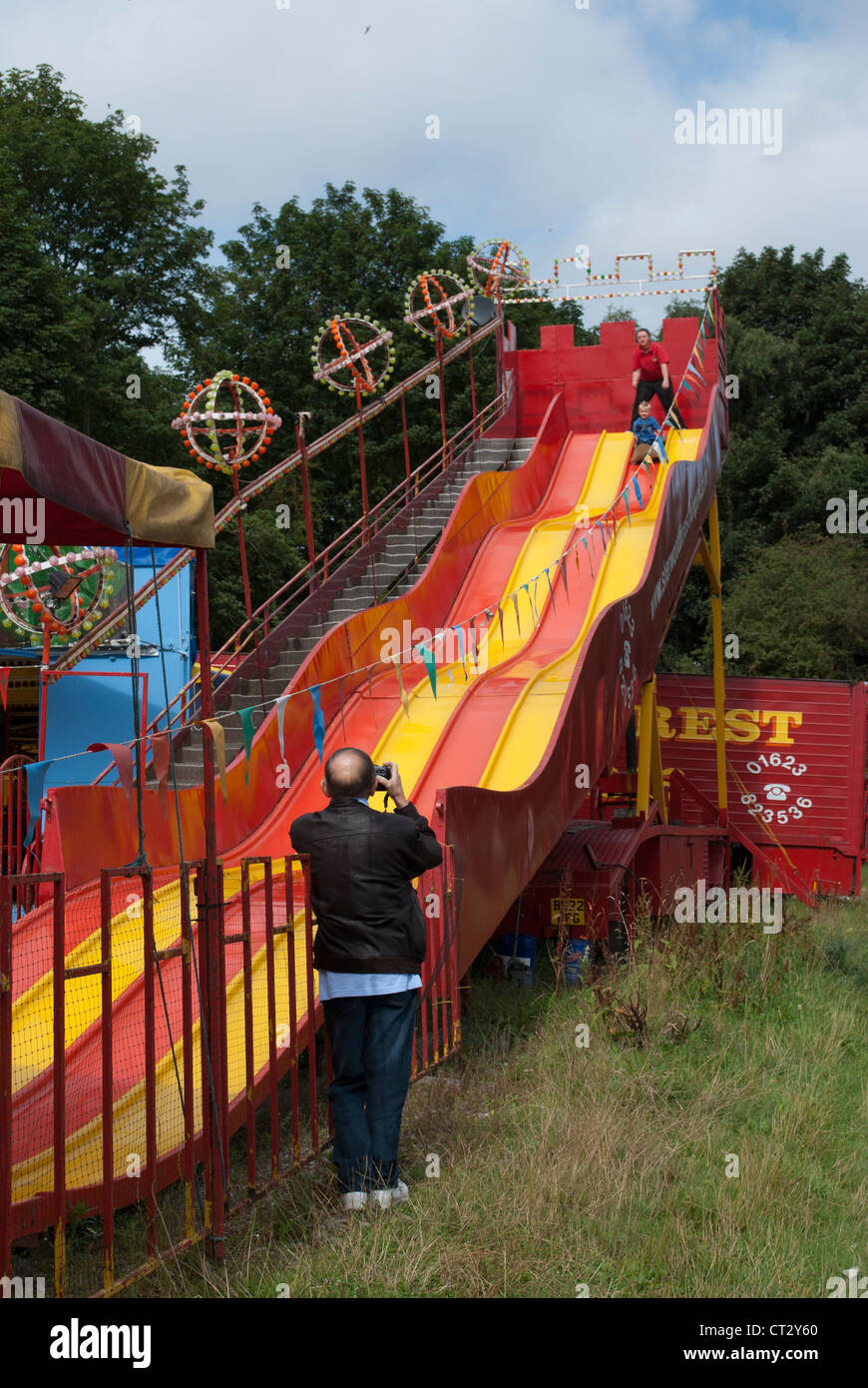 Man taking photograph at bottom of slide while child is held at the top ...
