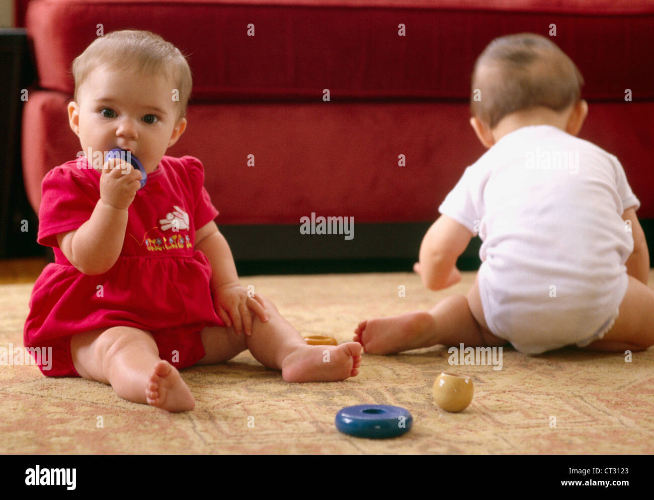 Two babies sitting on the floor playing together while one puts a toy ...