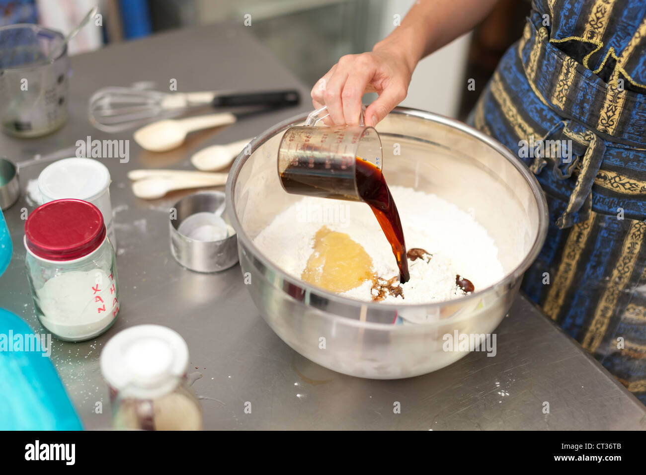 A woman pours as she mixes together ingredients in a large mixing bowl ...