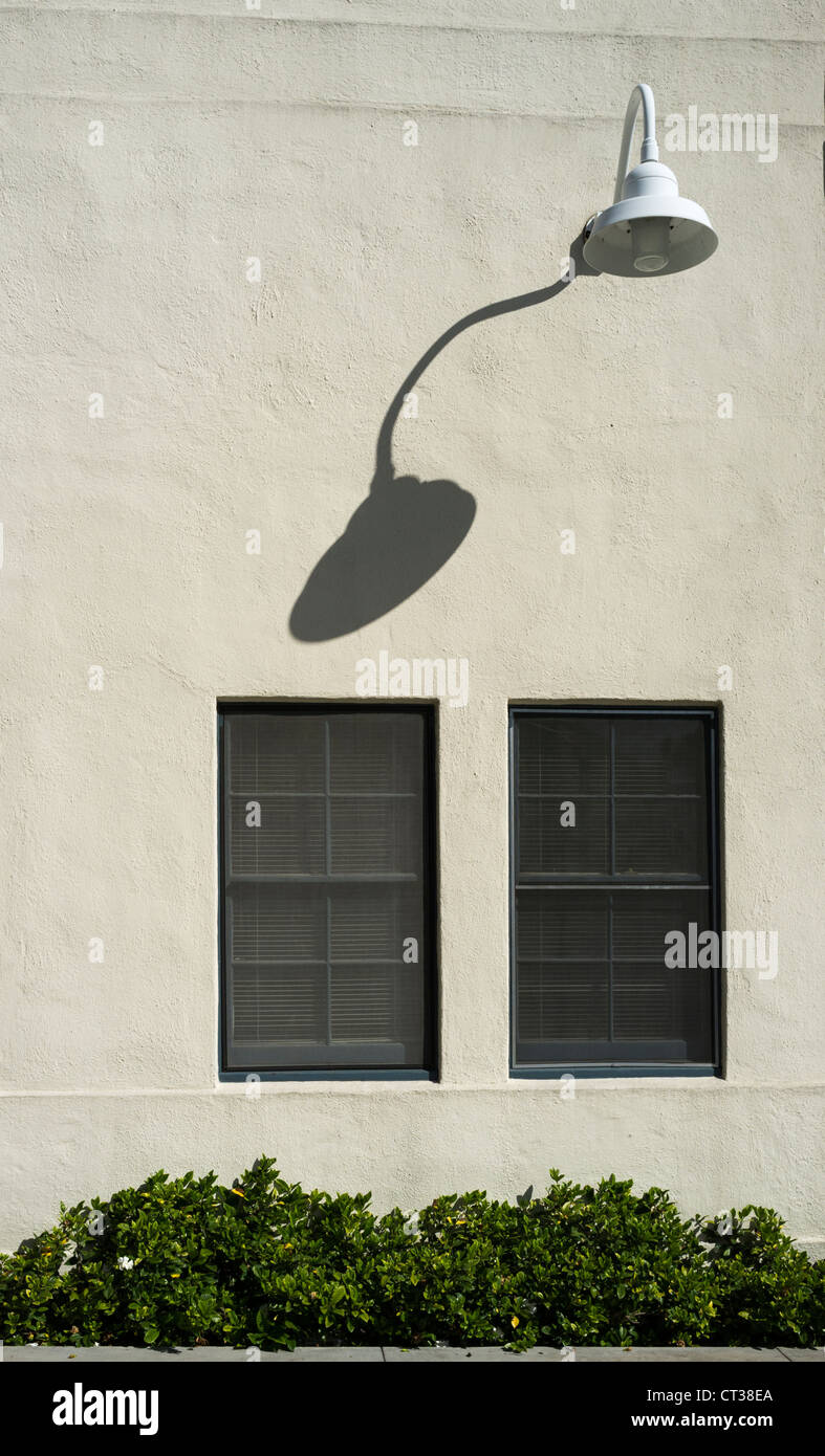 A wall lamp casting a strong shadow over a window on a plain art deco ...