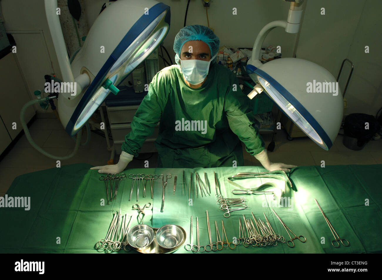 A masked surgeon leaning on a table of sterile surgical tools in a ...