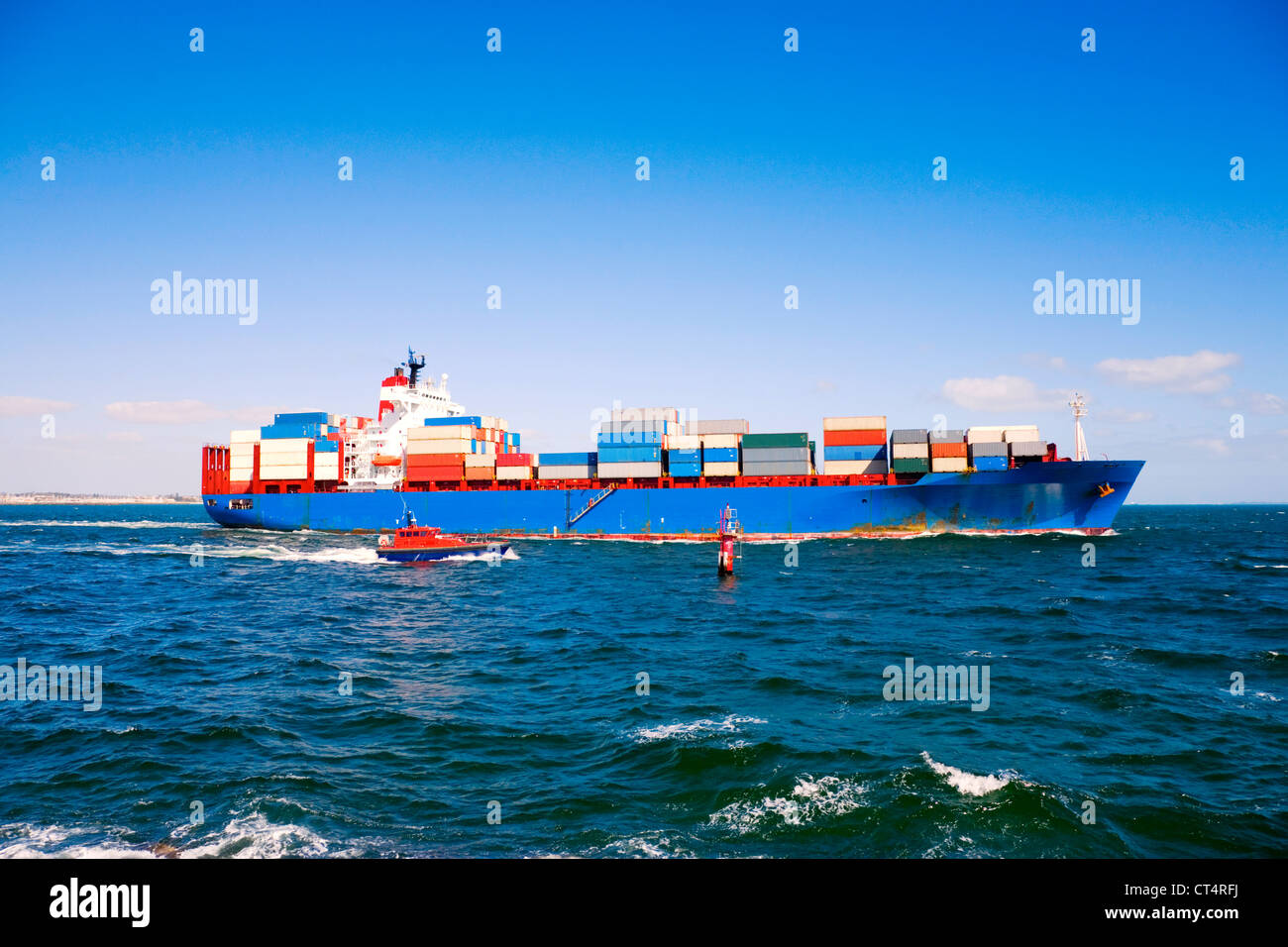 Pilot boat guiding huge container ship through deep water channel as it ...