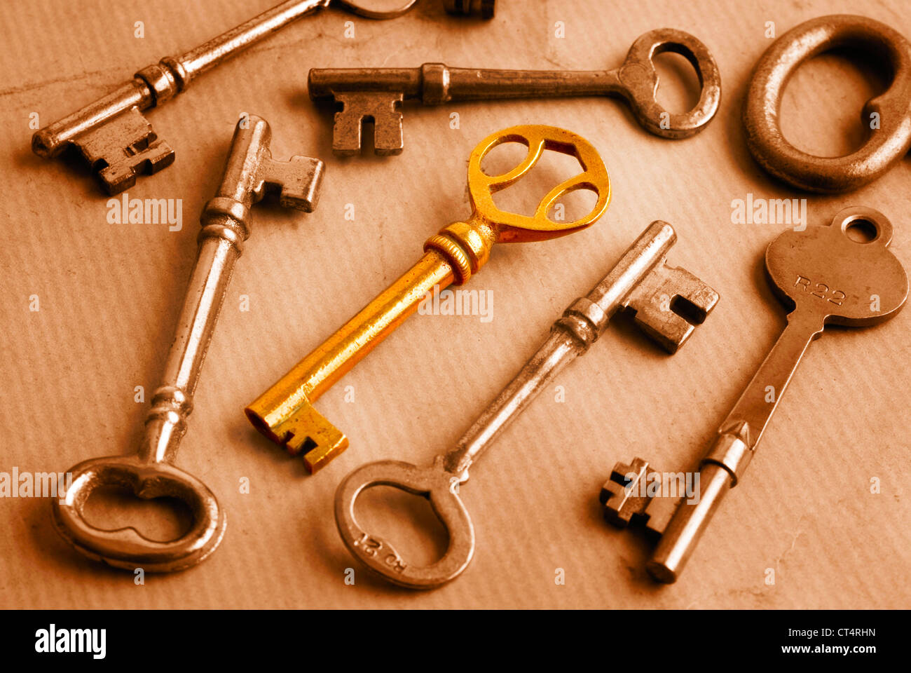Shiny golden key amongst old steel keys on worn paper background ...