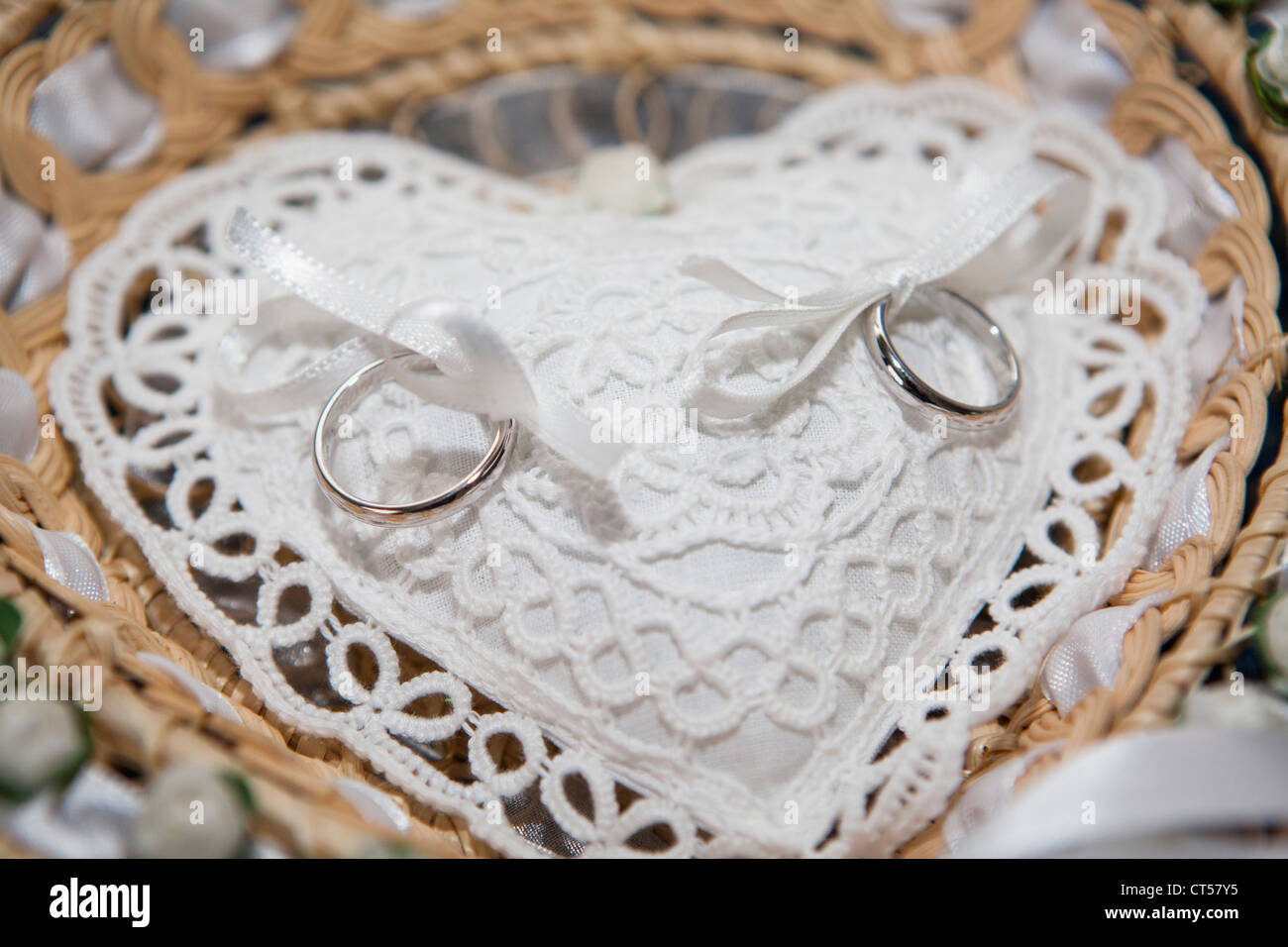 Wedding rings in a wicker basket with a white embroidered cushion close ...