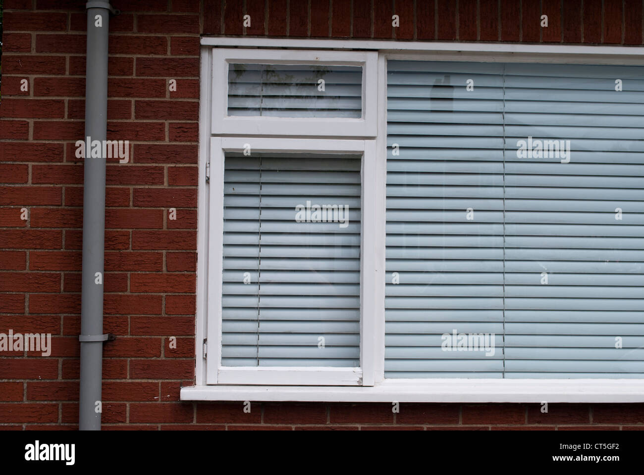 White framed window with closed white venetian blind in red brick wall ...