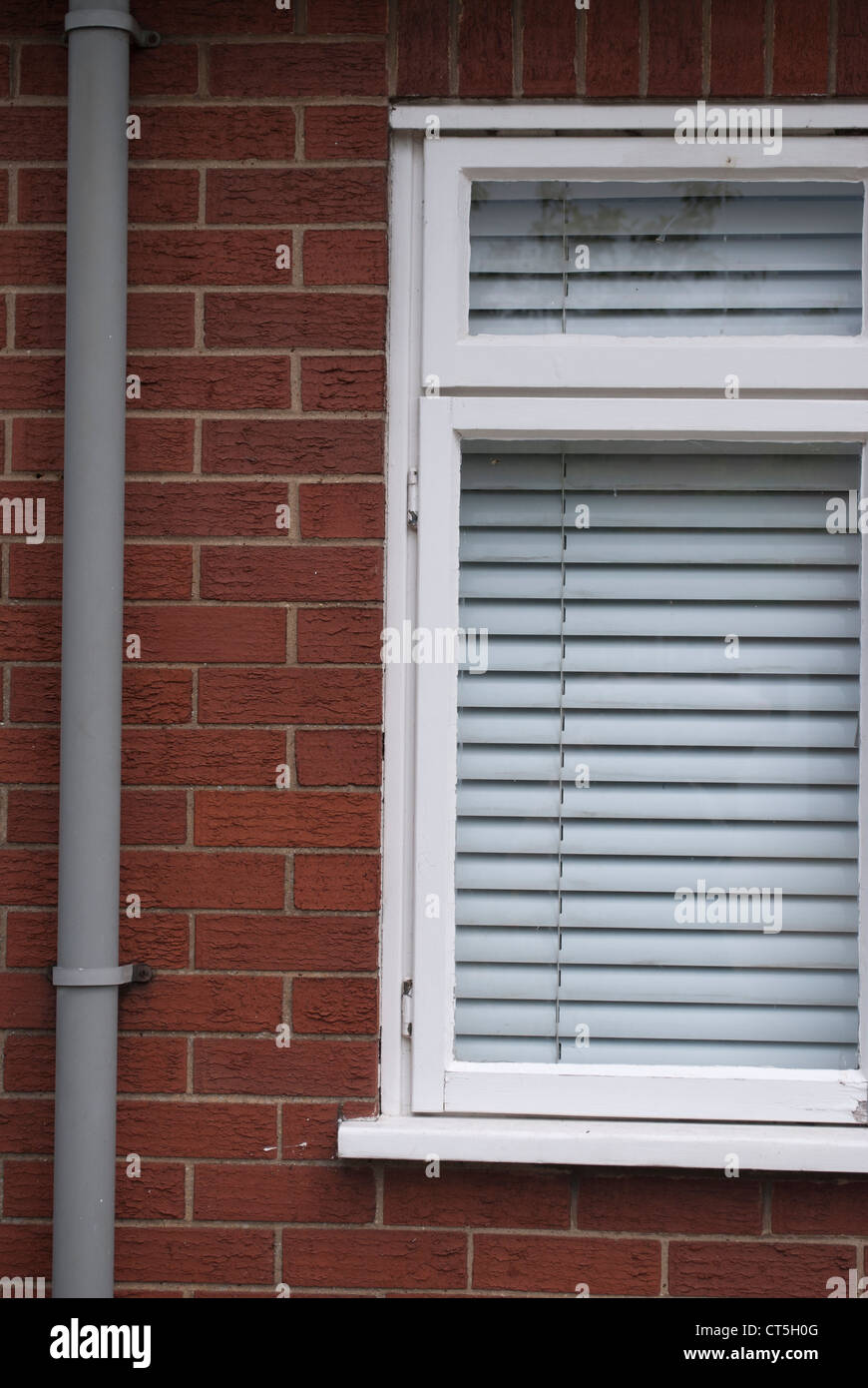 White framed window with closed white venetian blind in red brick wall ...