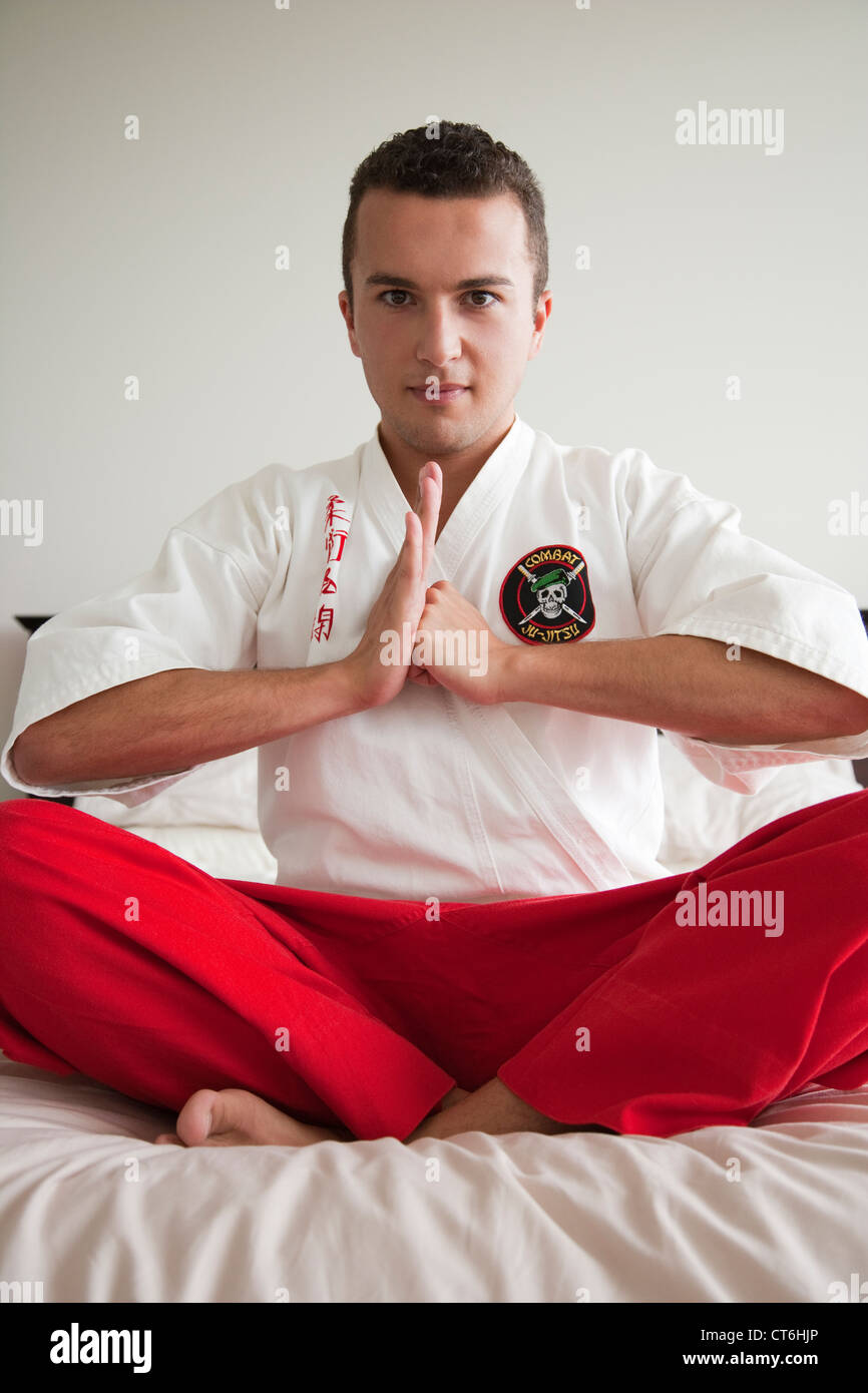 Portrait of a confident young man sitting in kung fu position on bed ...