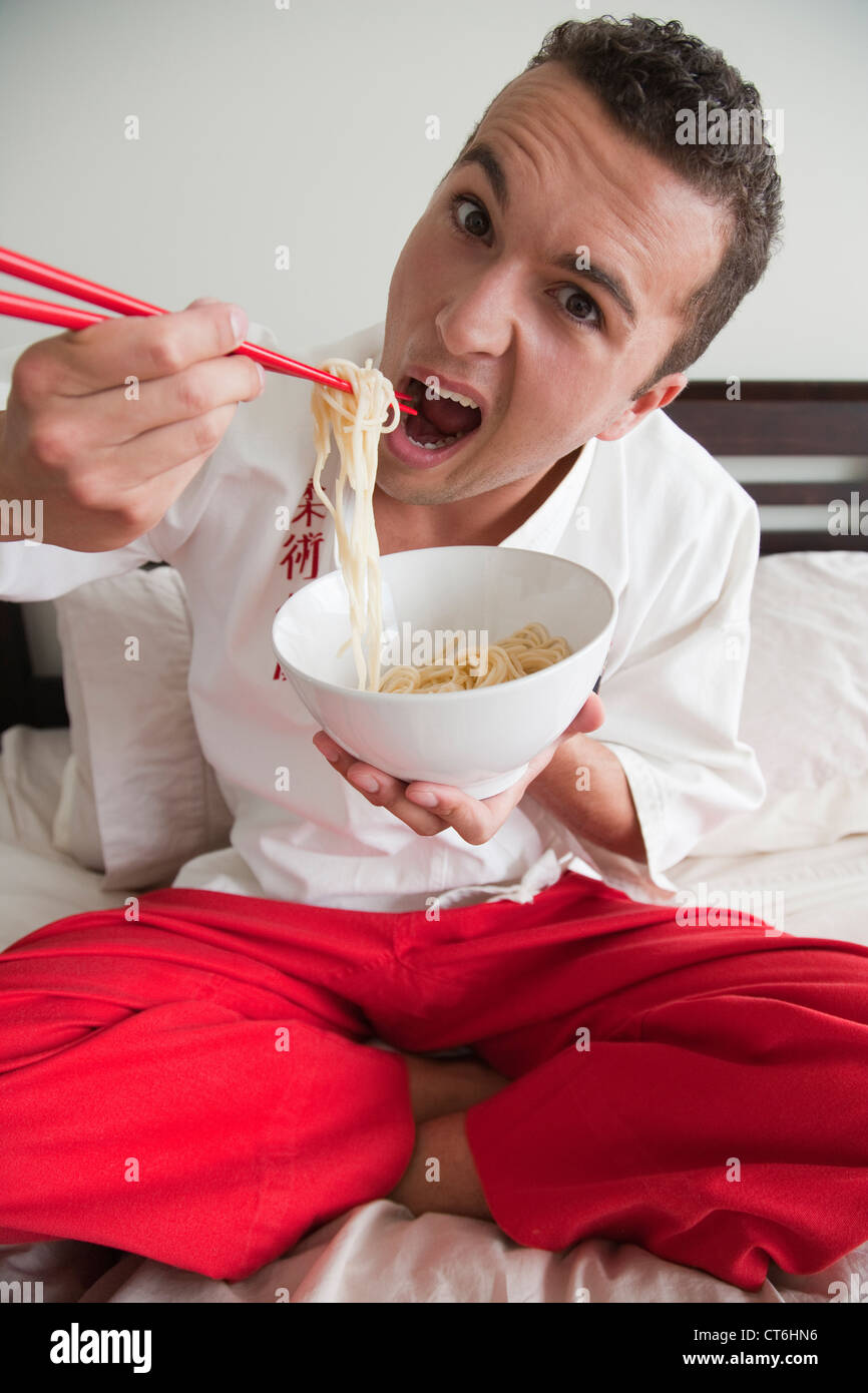 Portrait of a young man eating a bowl of noodles using chopsticks Stock ...