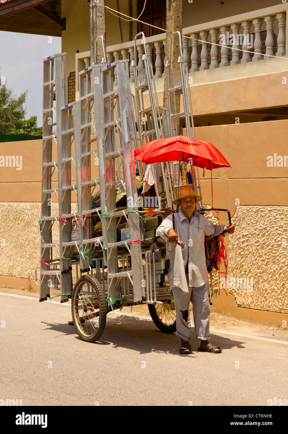 Thai man pulling a cart laden with Aluminium ladders which he is ...