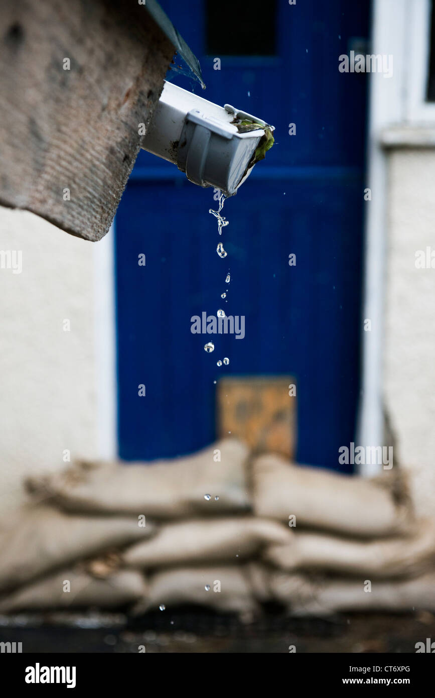 Rain dripping from guttering outside house with sandbags in the doorway ...