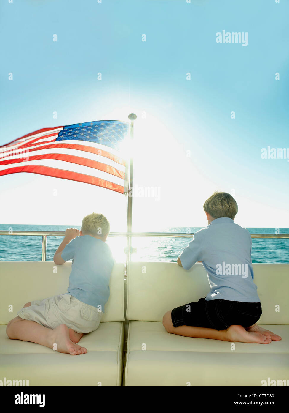 Boys in the back of a yacht with american flag, looking out to sea ...