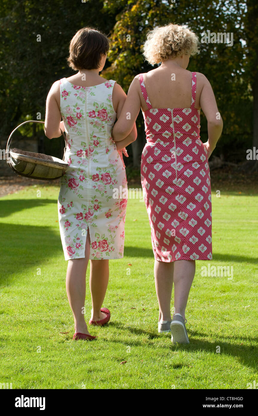 Two women walking arm in arm across a lawn carrying a basket Stock ...