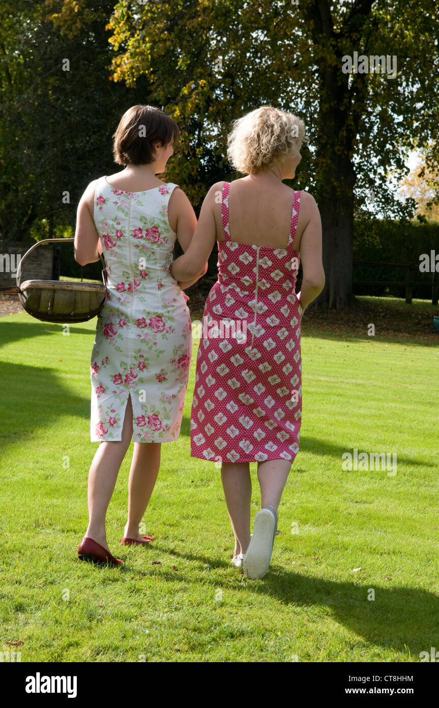 Two women walking arm in arm across a lawn carrying a basket Stock ...