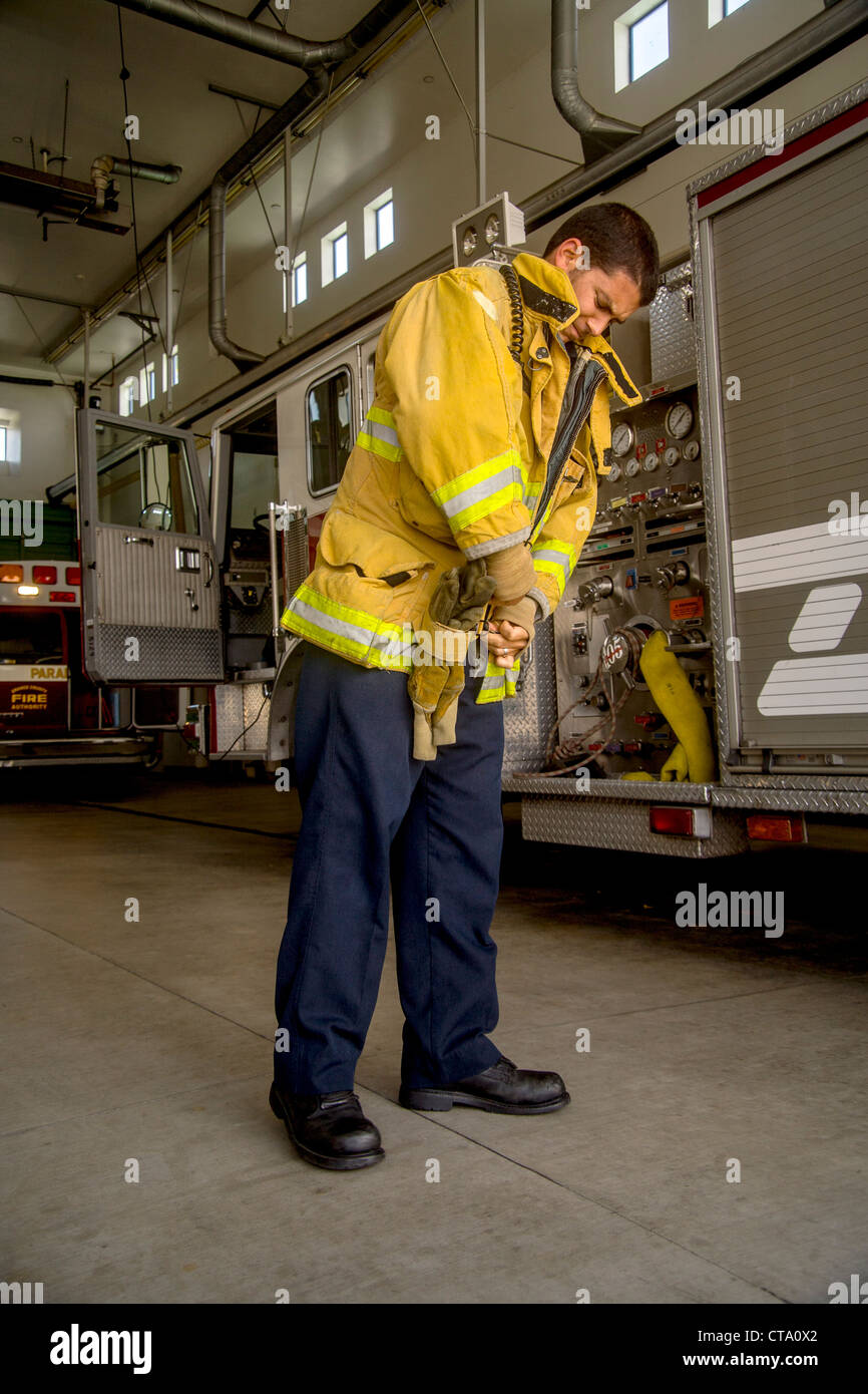 Wearing his helmet, a young firefighter dons his yellow safety jacket ...