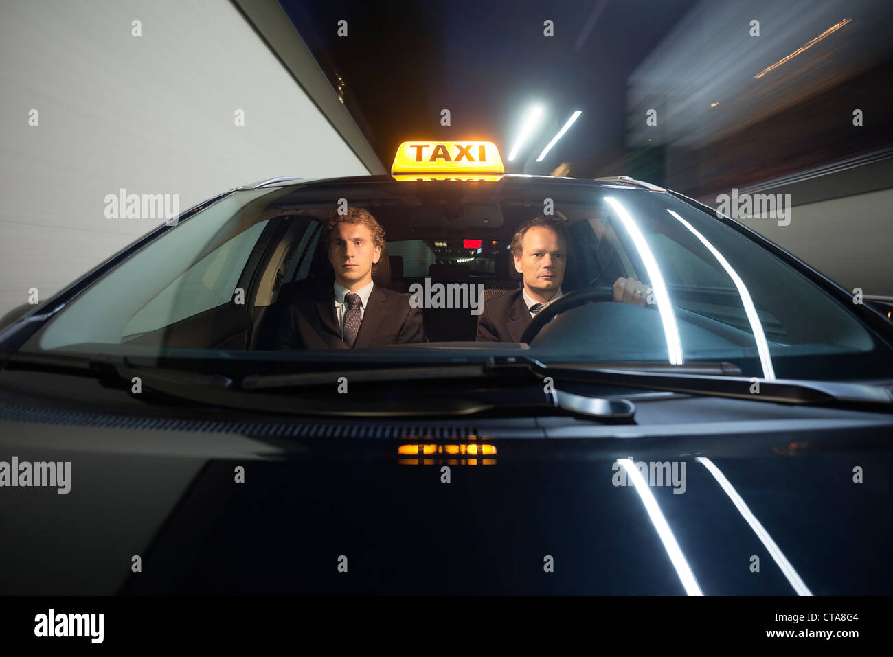 Taxi driver and passenger inside a cab, driving at high speed at night ...