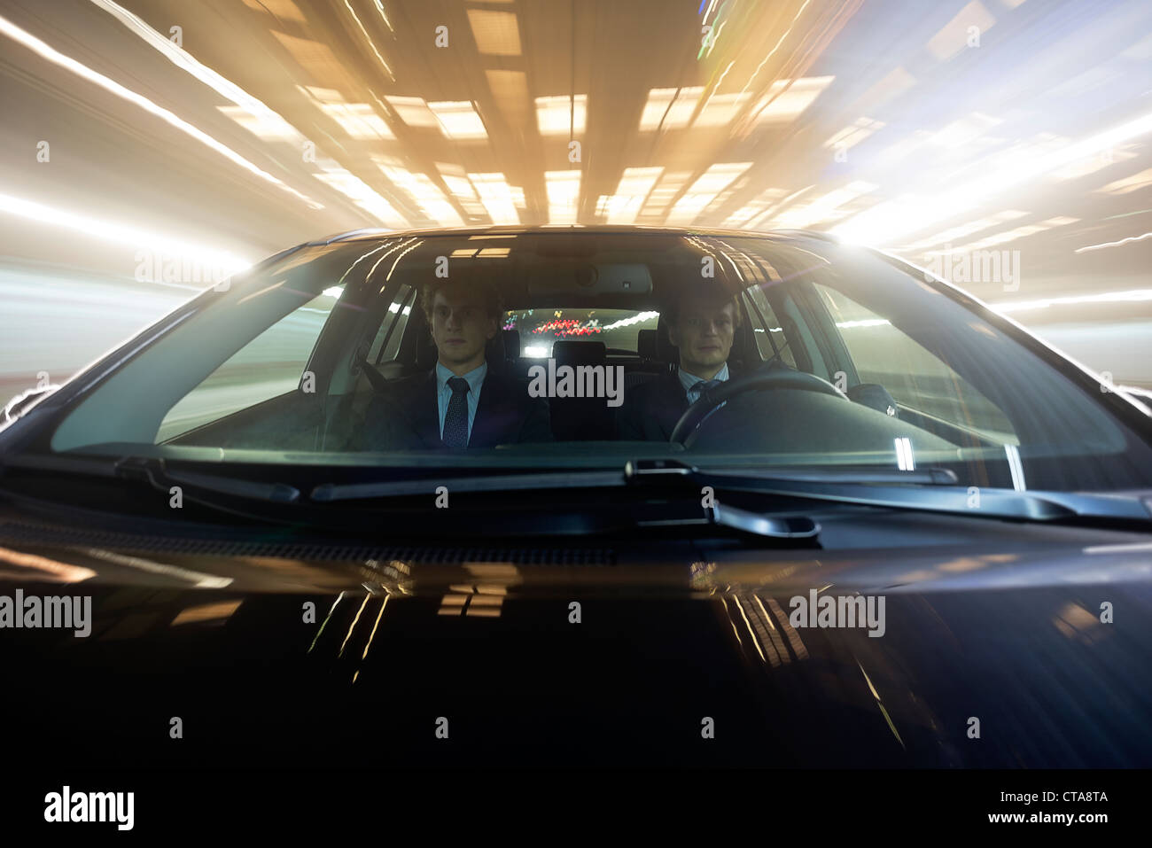 Two businessmen in a car, driving through a tunnel, seen from the hood ...
